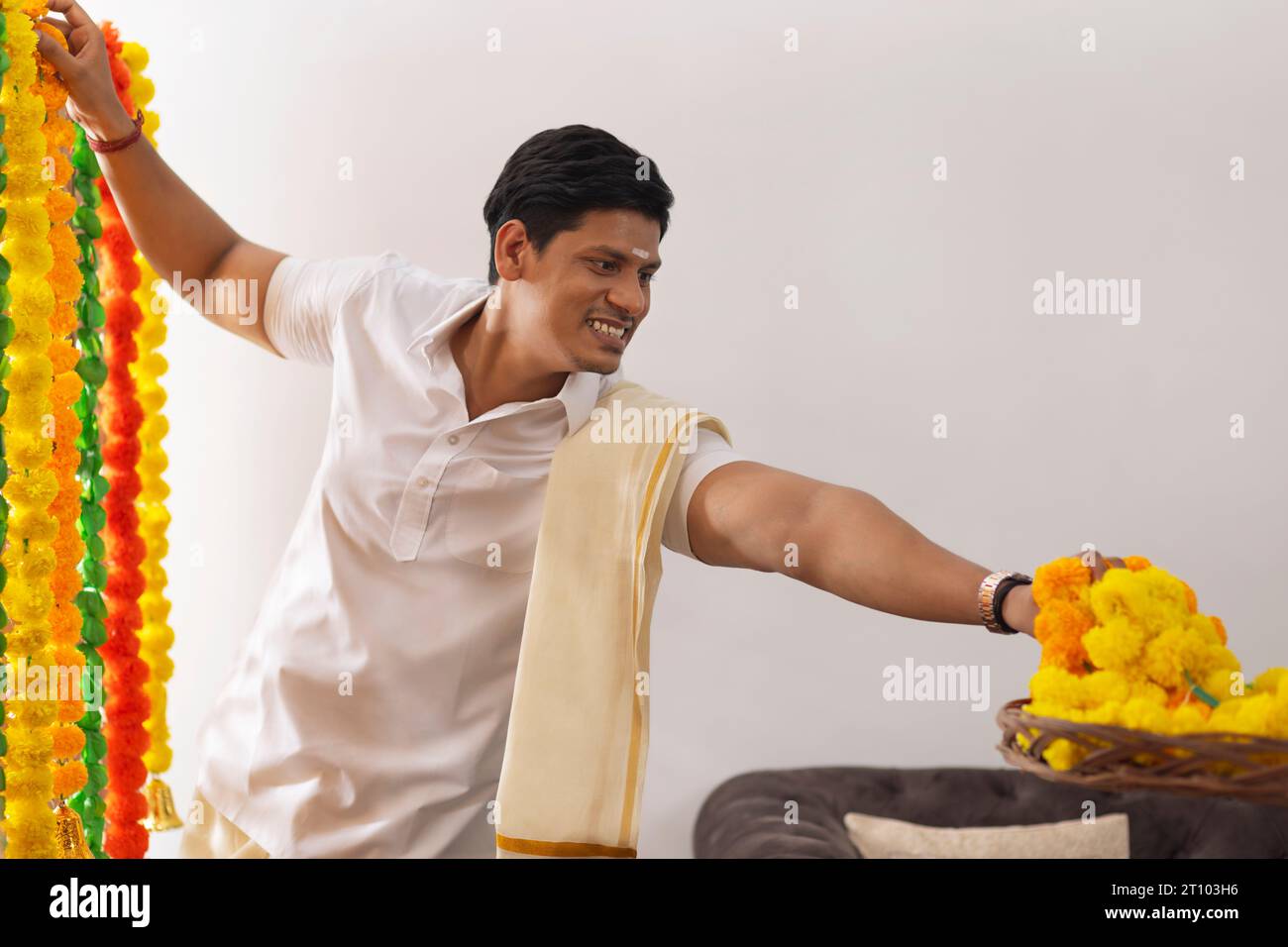 South Indian man decorating house with flower garland to celebrate Onam ...