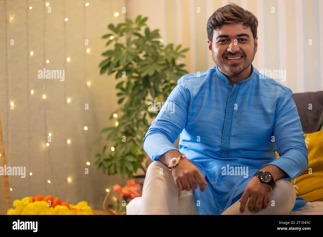 Portrait of cheerful young man in traditional outfit sitting at home on ...