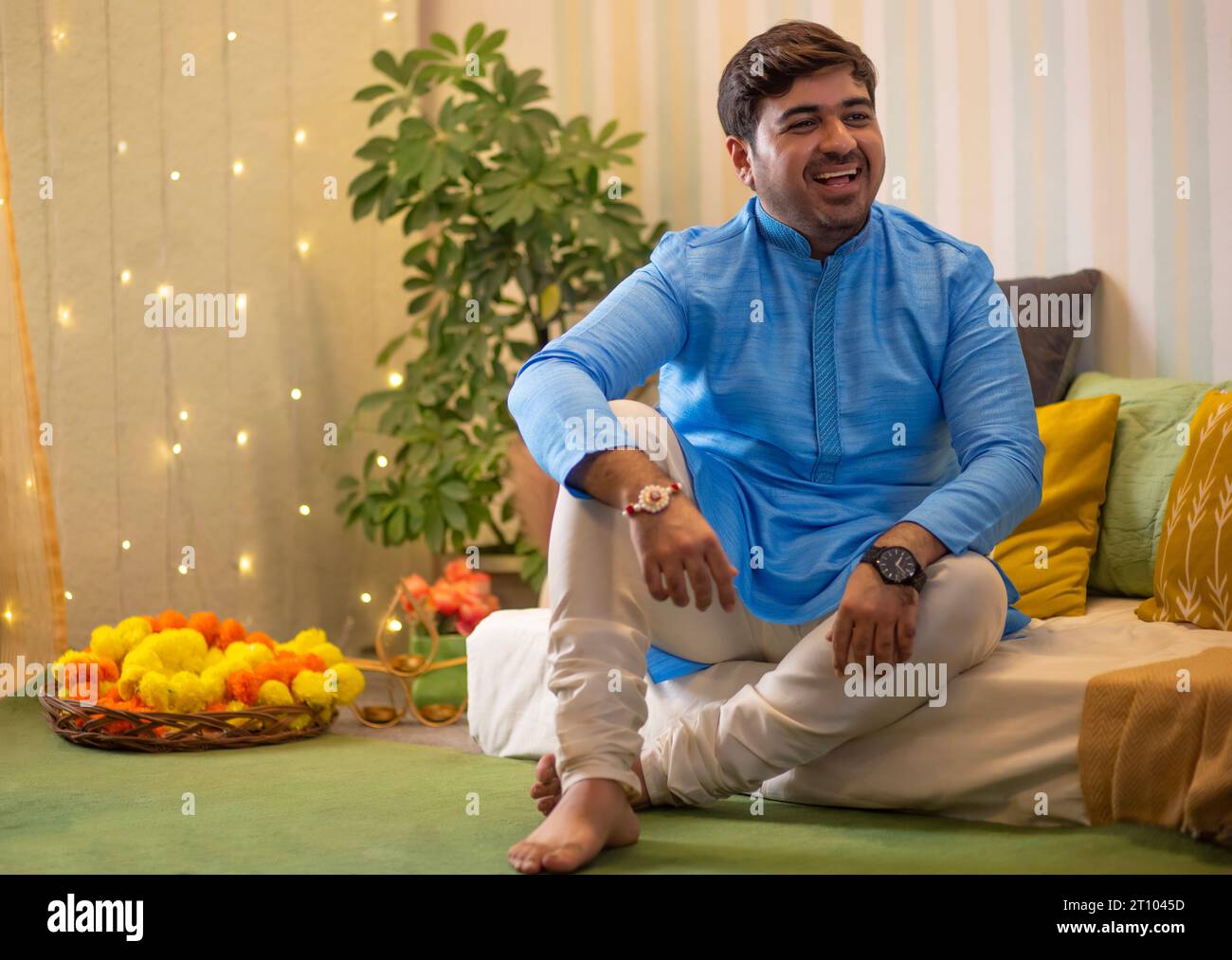 Portrait of cheerful young man in traditional outfit sitting at home on ...