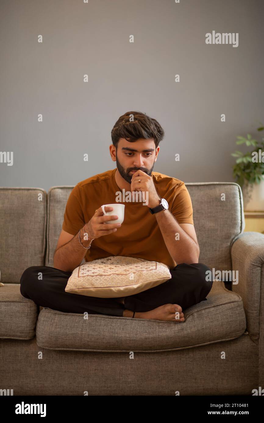 Young man drinking tea while relaxing on sofa in living room Stock ...