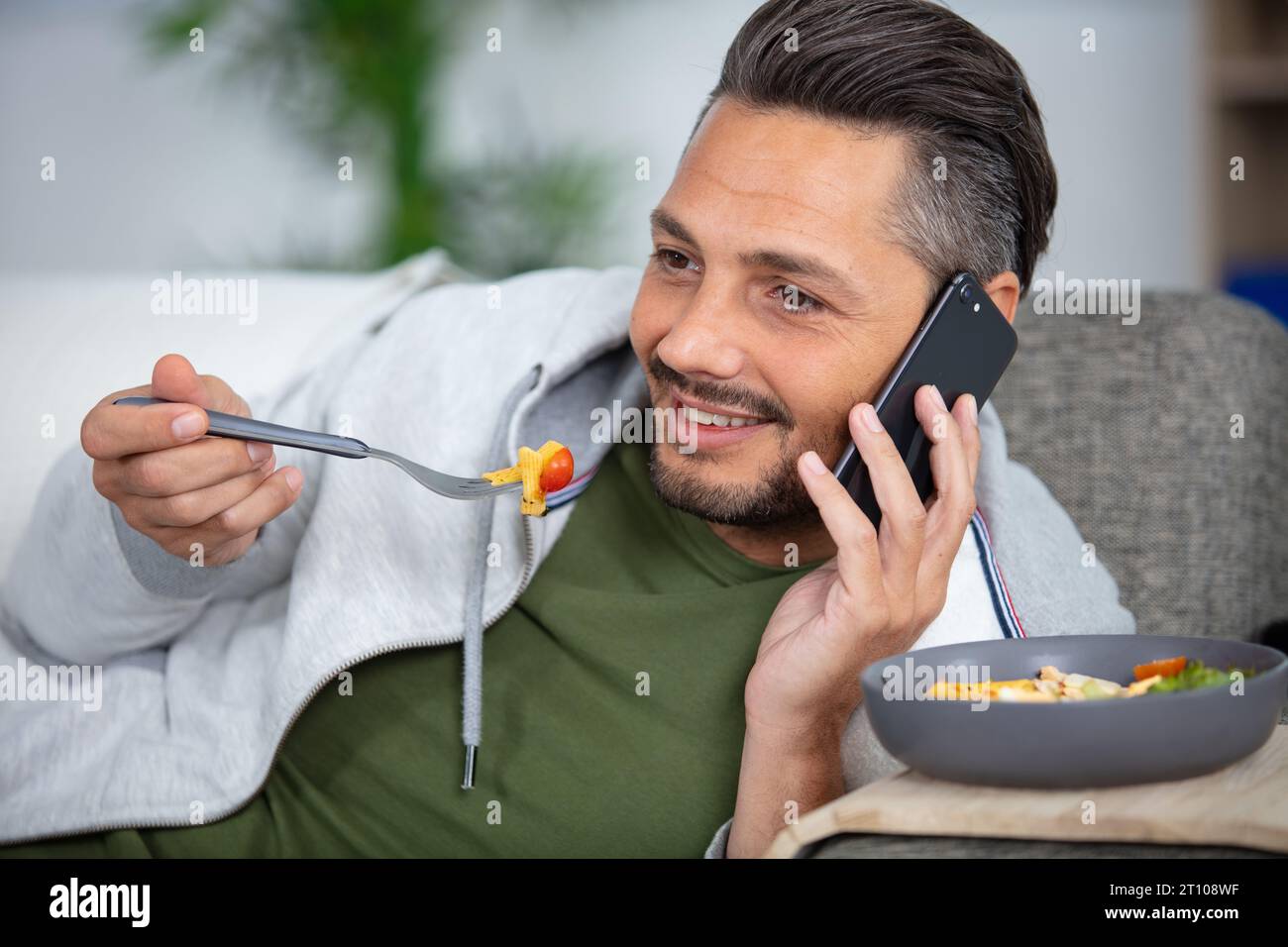 guy sitting on sofa eating salad while talking on smartphone Stock ...