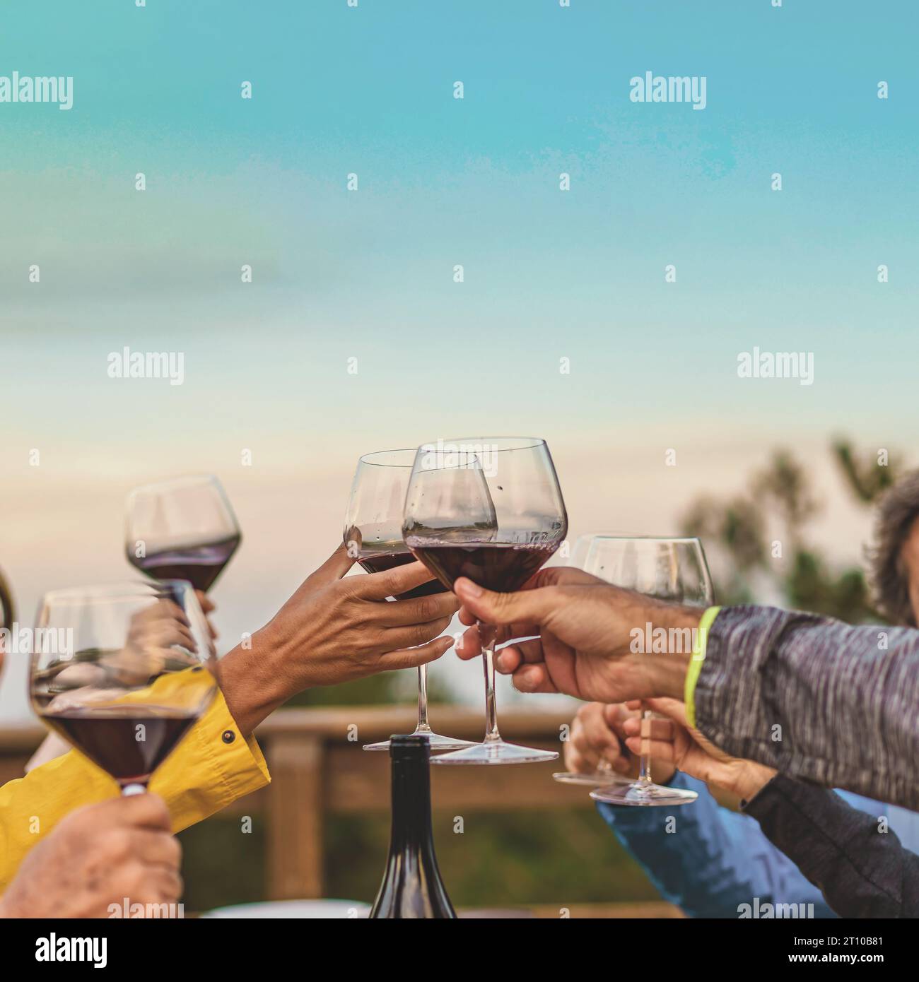 Close-up of raised wine glasses toasting at sunset outdoors. Square ...