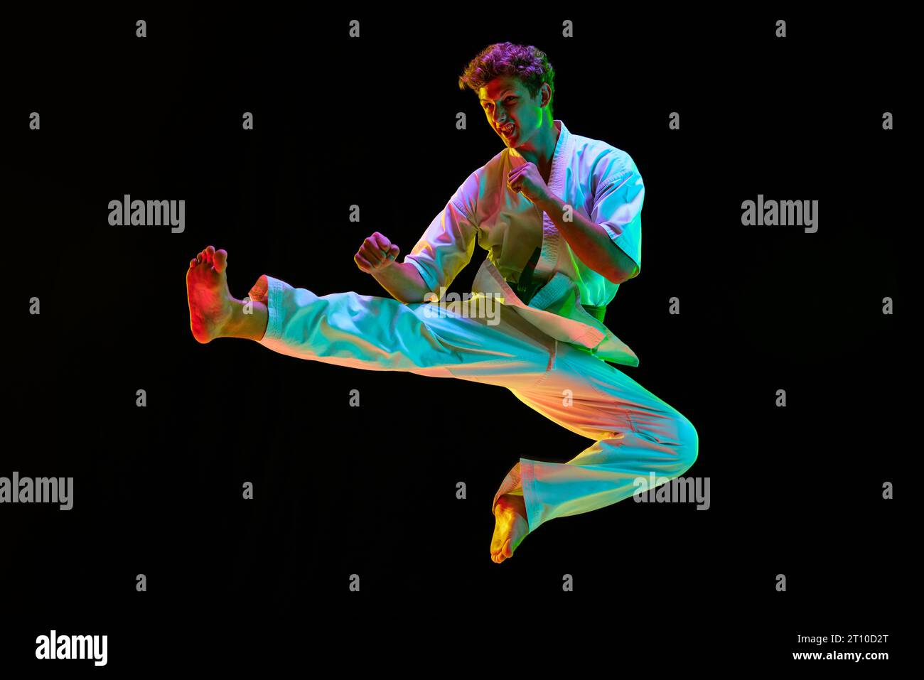 Young sportive man, karateka in white kimono training over black studio ...