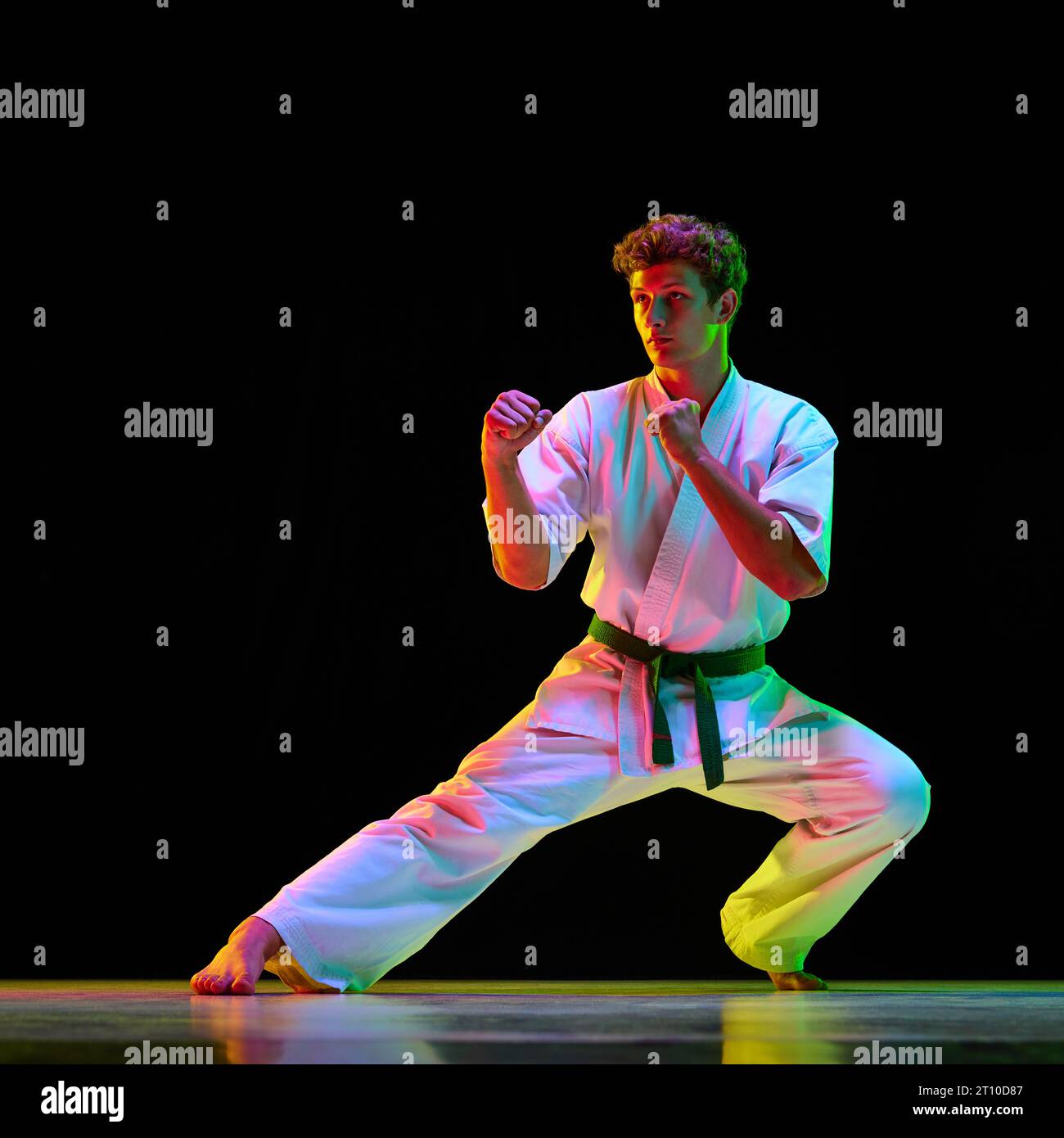 Defense pose. Young guy in white kimono practicing over black studio ...
