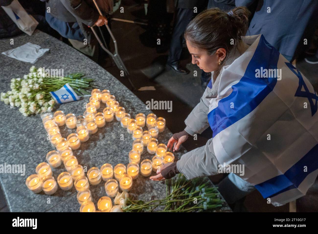 A woman draped with Israeli flag takes care of the makeshift memorial ...