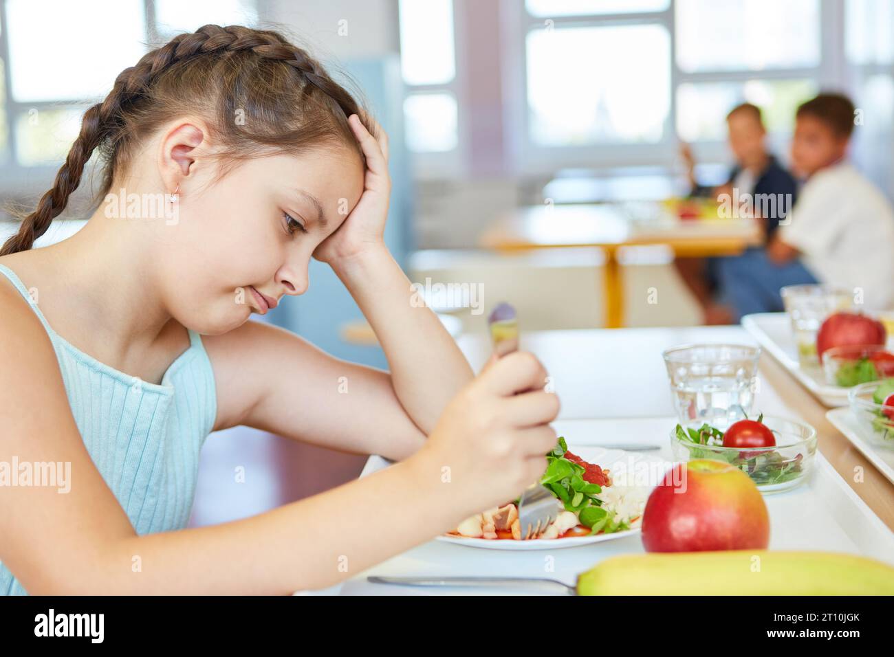 Tired girl with head in hand staring at food plate during lunch time in ...