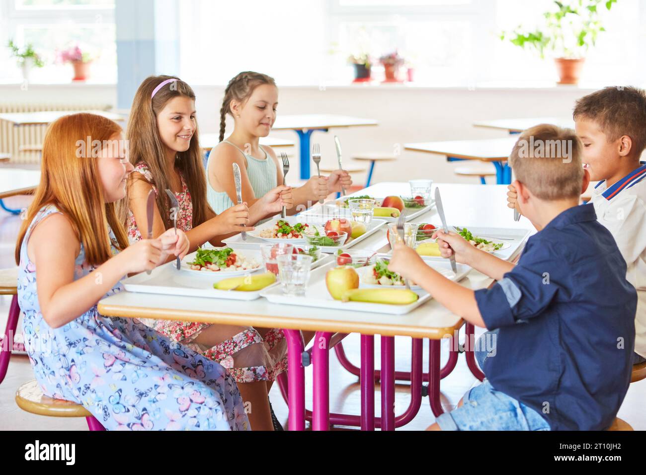Smiling school children holding cutlery while sitting at table during ...