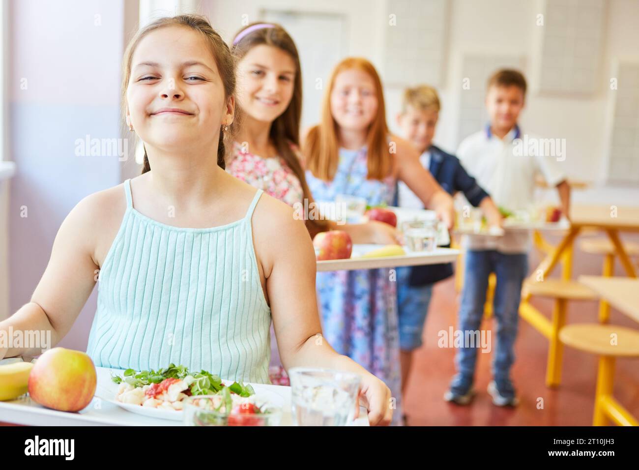 Smiling female students standing in line holding food trays during lunch time in school ...