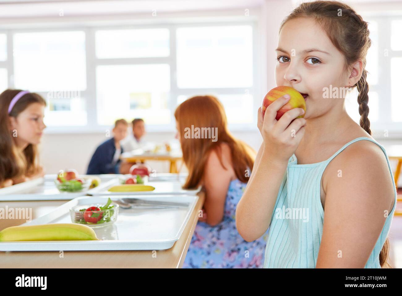 Portrait of girl eating fresh apple sitting with friends in cafeteria ...