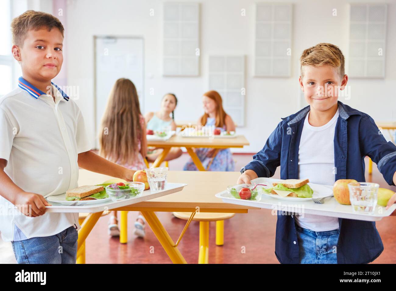 Portrait of smiling schoolboys holding food trays during lunch time in ...