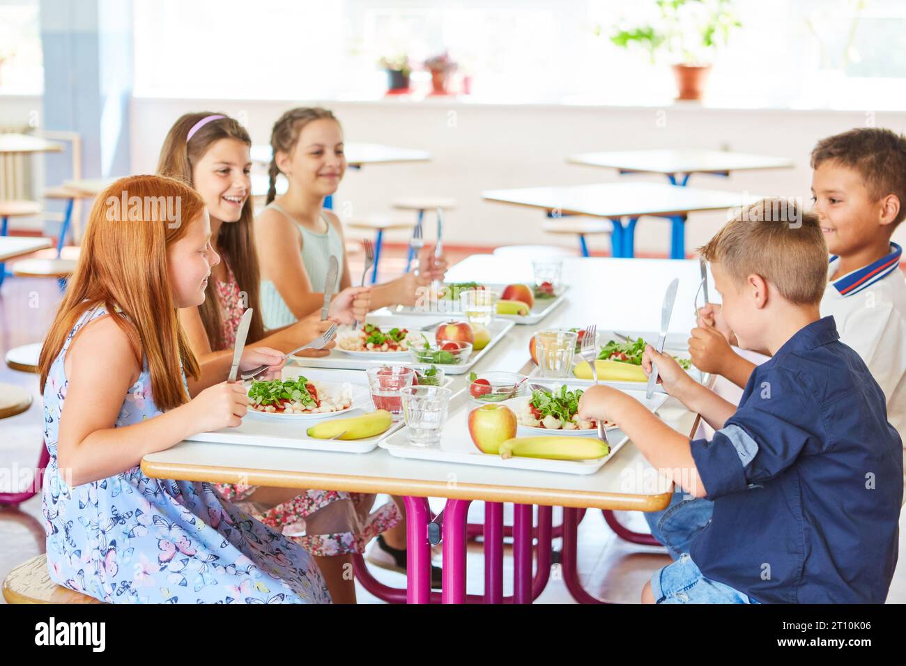 Happy kids having meal with cutlery while sitting together at table in ...
