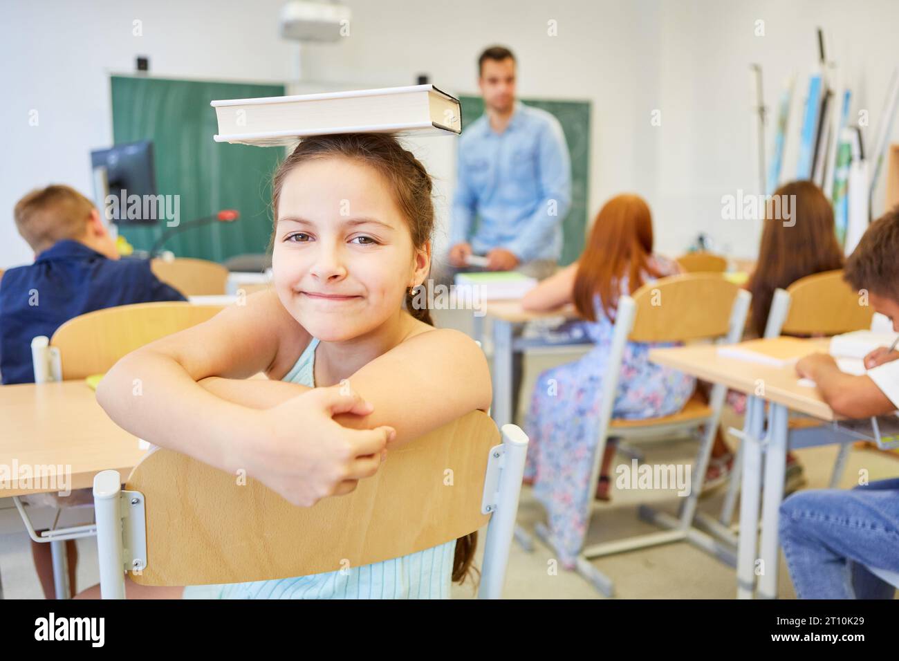 Portrait of smiling elementary student balancing book on head while ...