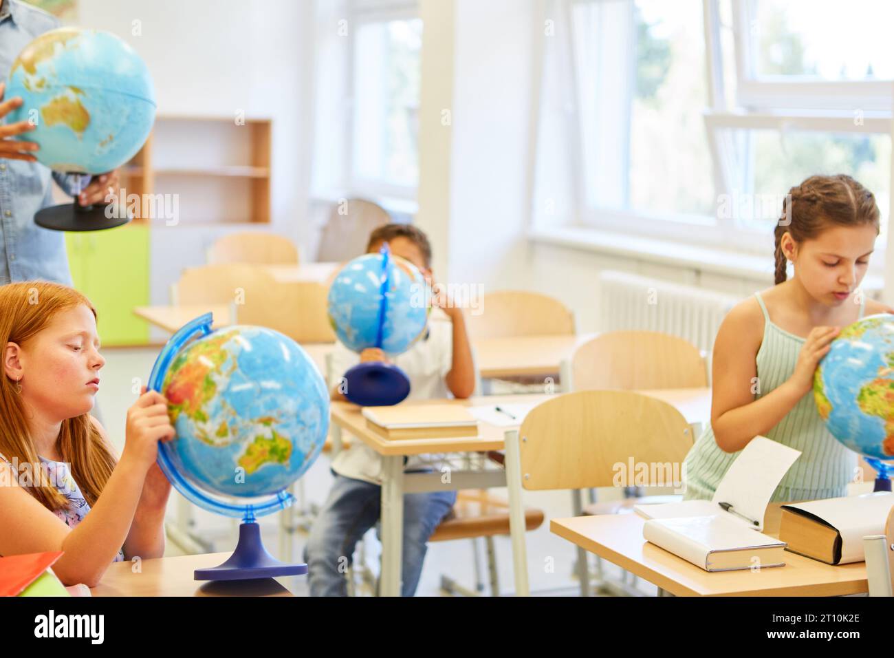 Elementary students examining globes during geography lecture in class ...