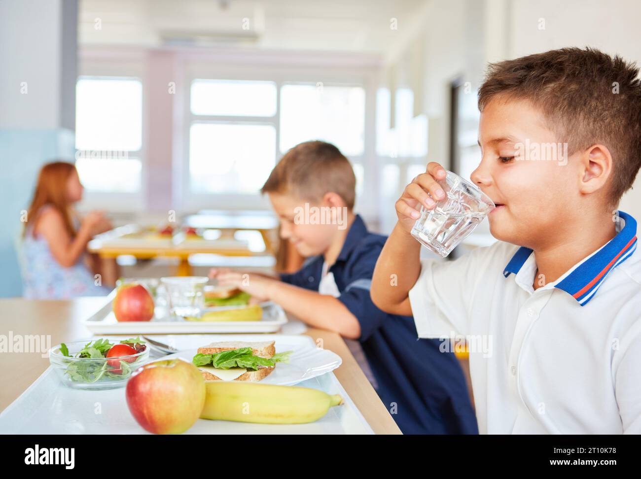 Schoolboy drinking water from glass while having lunch in cafeteria ...