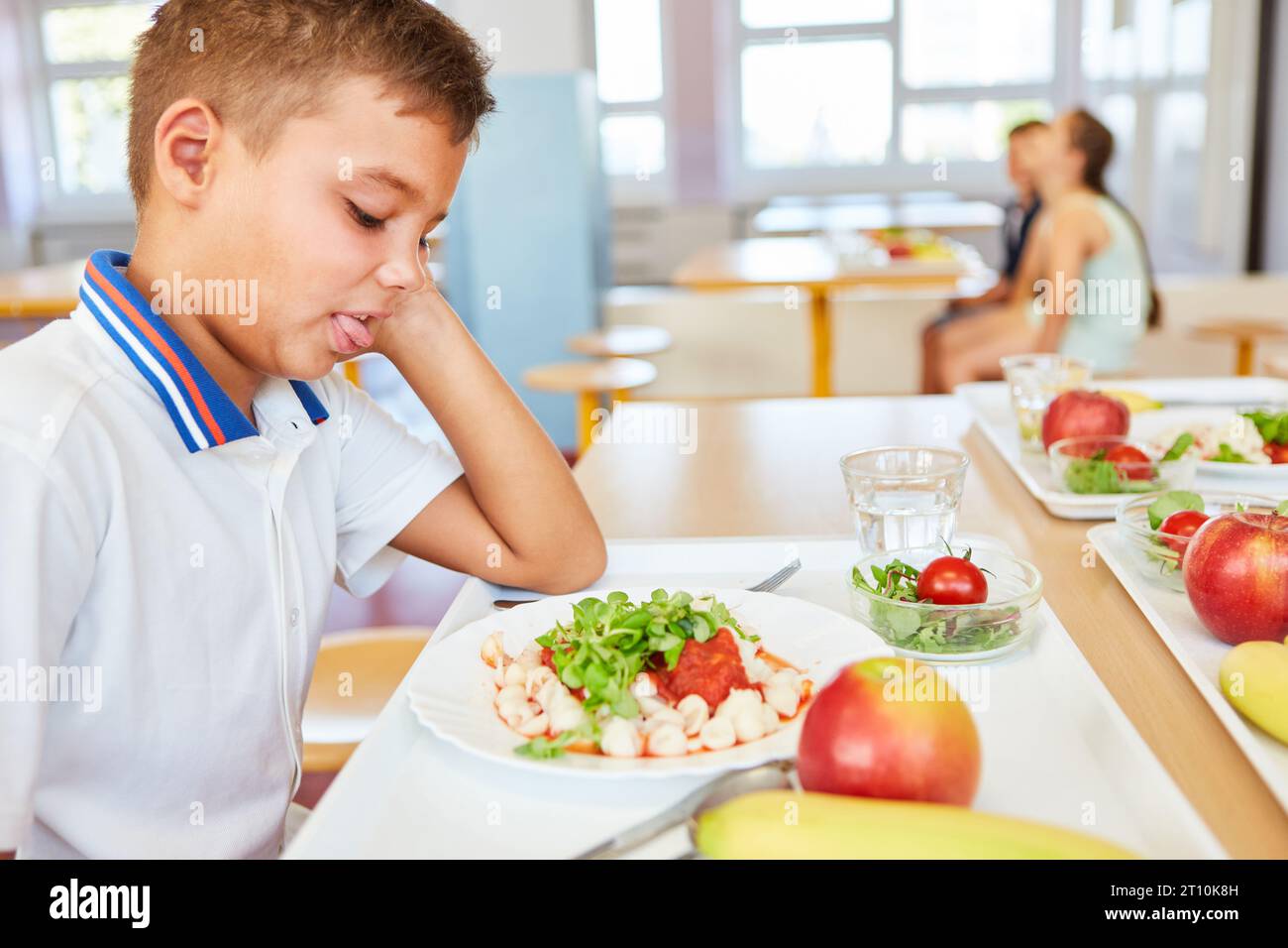 Boy sticking out tongue while staring at food plate during lunch time ...
