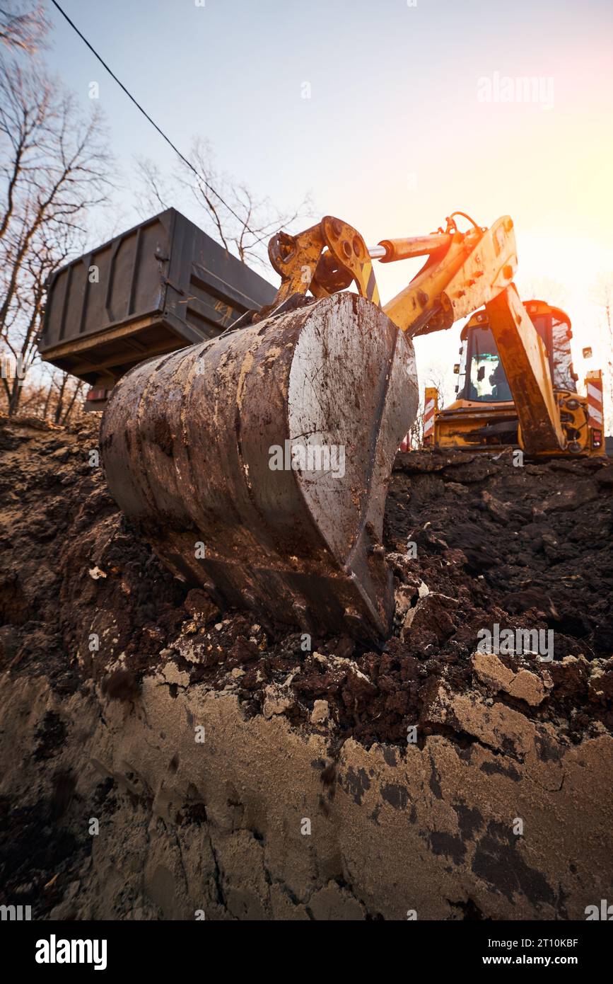 Excavator digs a hole in the ground to build a house at sunset, no ...