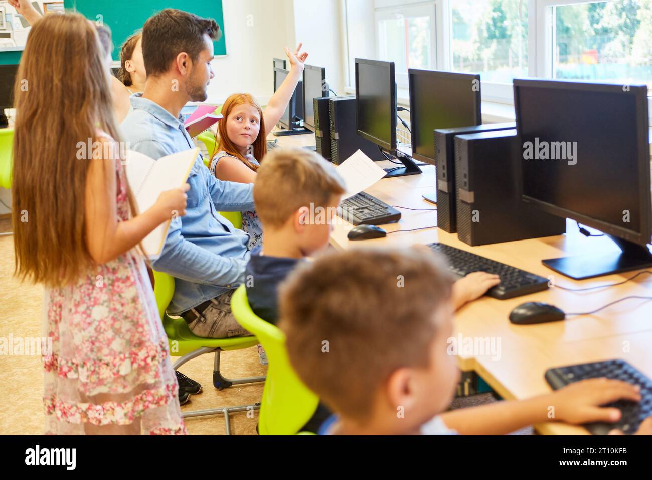 Male and female elementary students discussing with teacher in computer ...