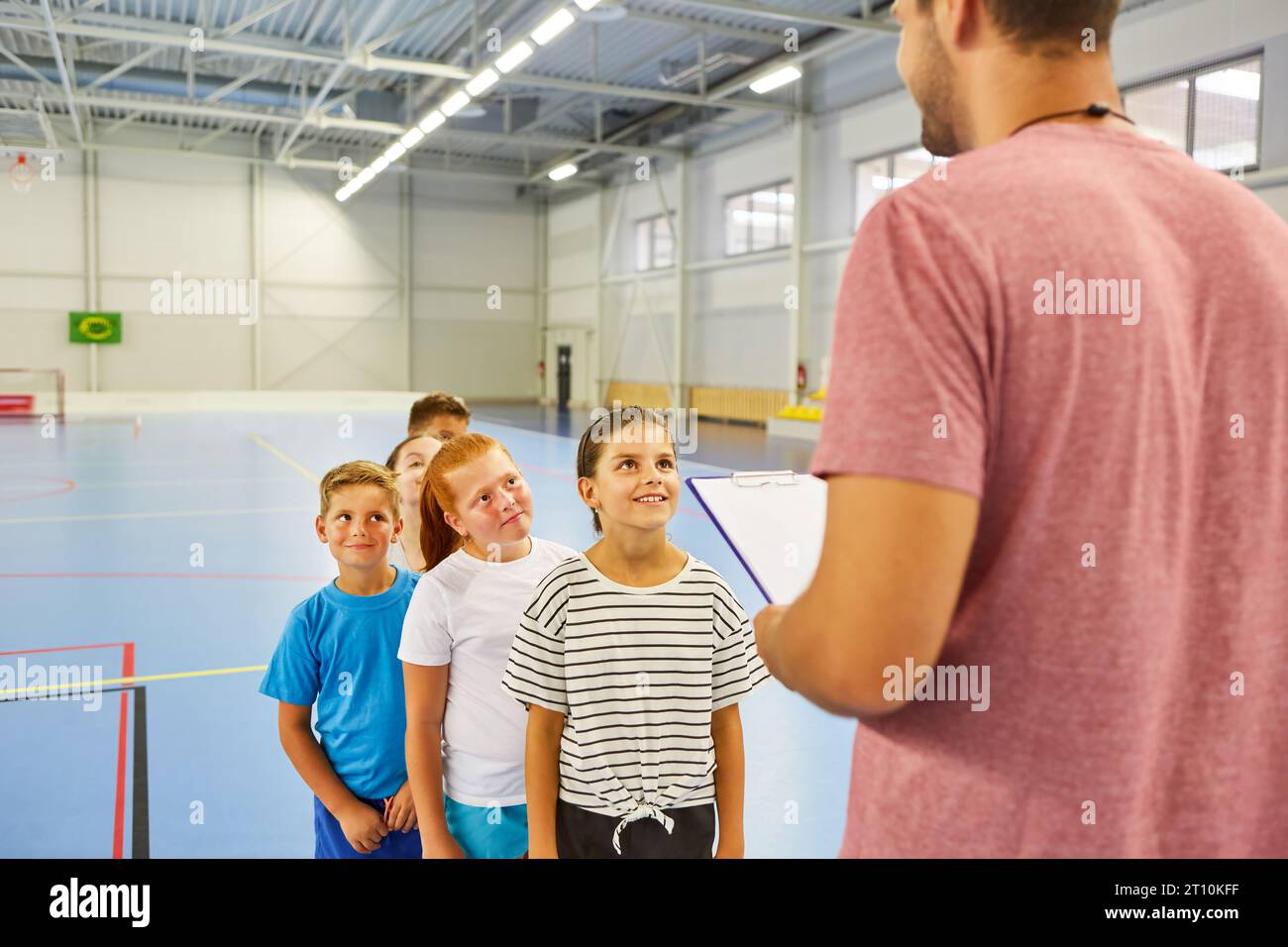 Male teacher talking to elementary students standing in line during gym ...