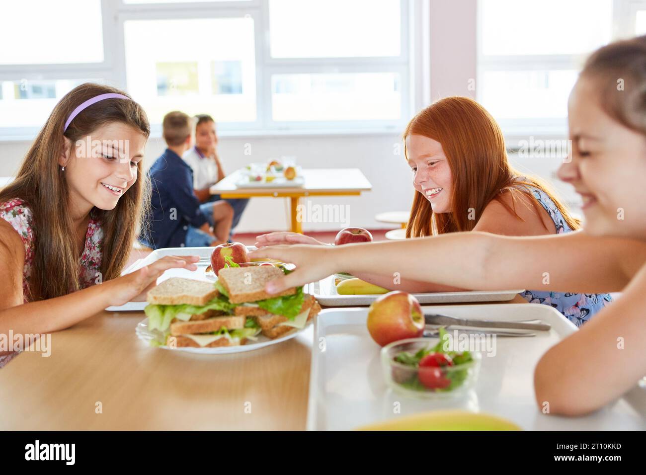 Happy female students picking up fresh sandwiches from table during ...