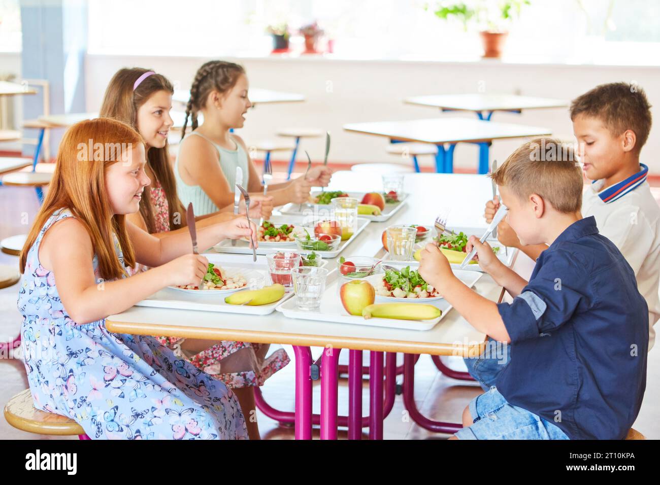 Group of happy elementary school children sitting at table eating food ...