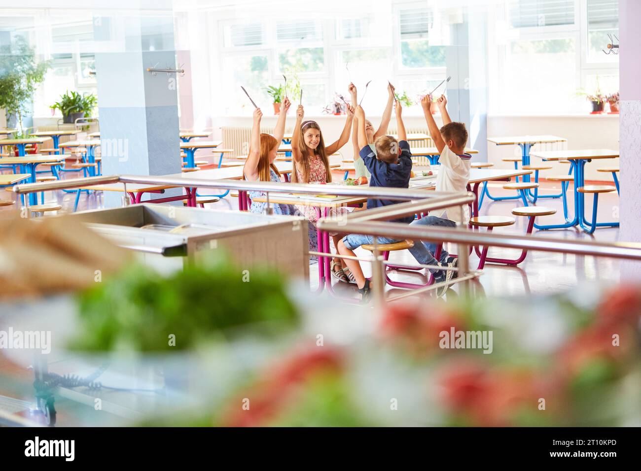 Cheerful male and female students with arms raised sitting together at table during lunch break ...