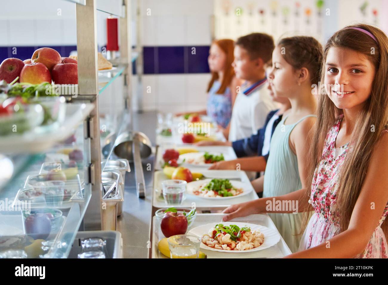Portrait of smiling girl with food tray standing in line by friends during lunch break in school ...