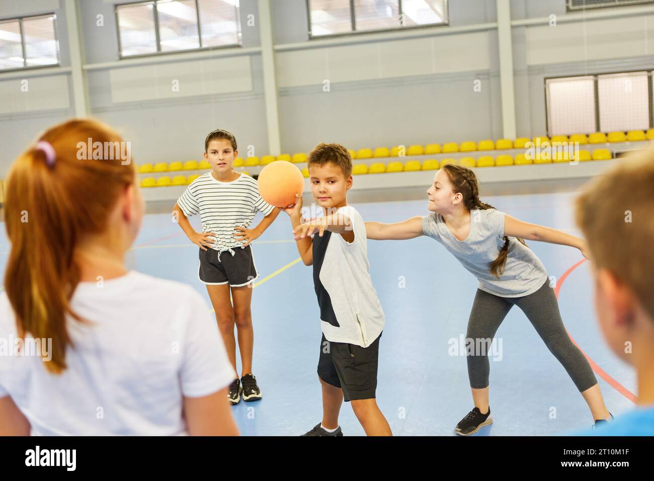 Male and female schoolkids playing with ball during gym class in school ...