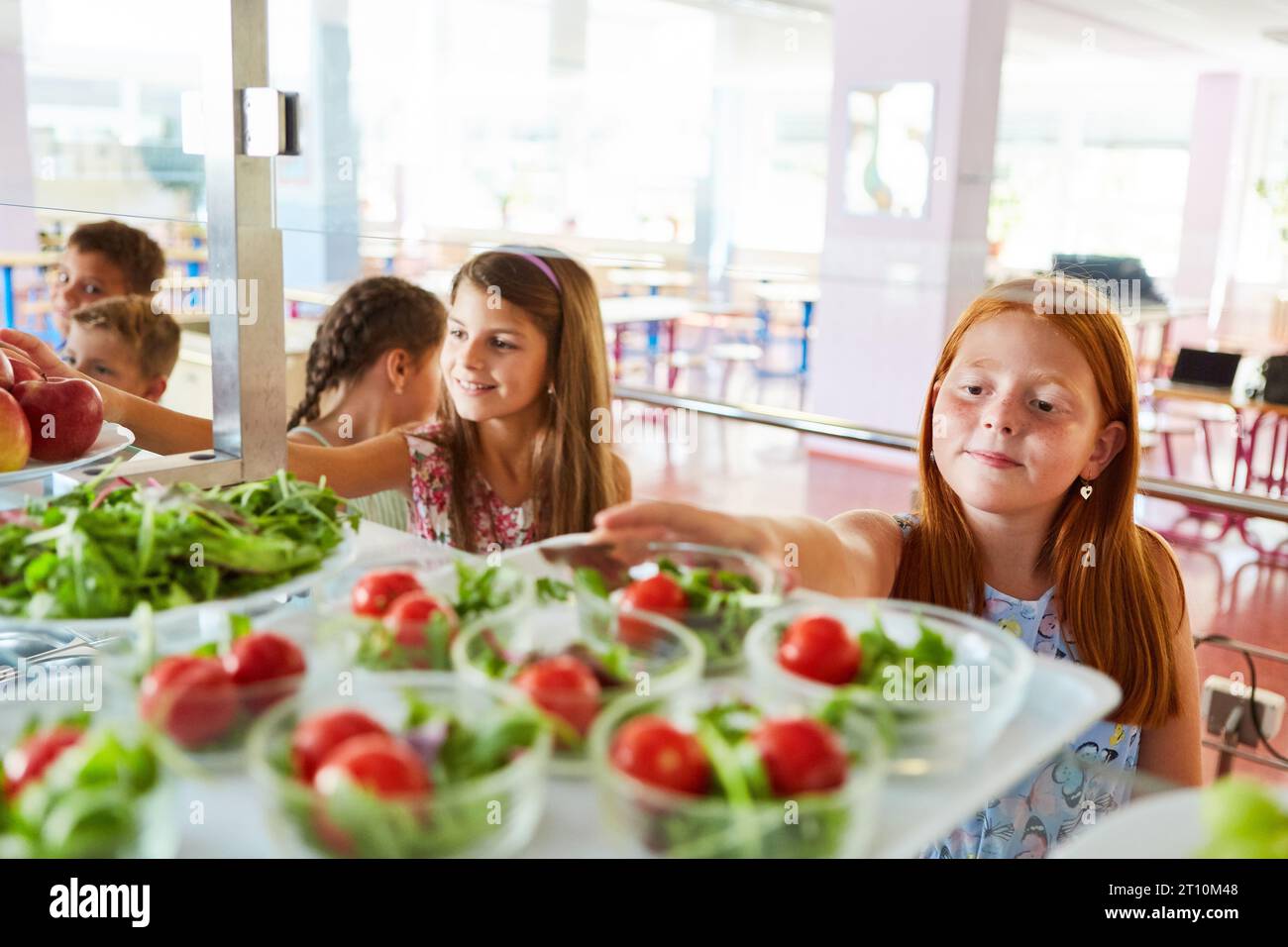 Male and female students taking food arranged in tray during lunch time in school cafeteria ...