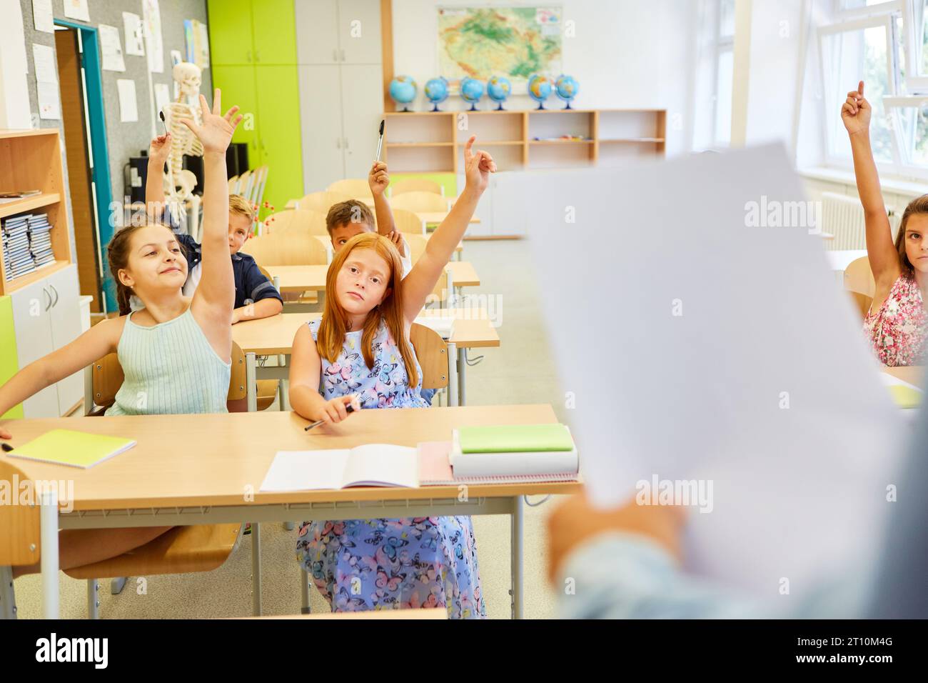 Male and female students raising hands while sitting together during ...