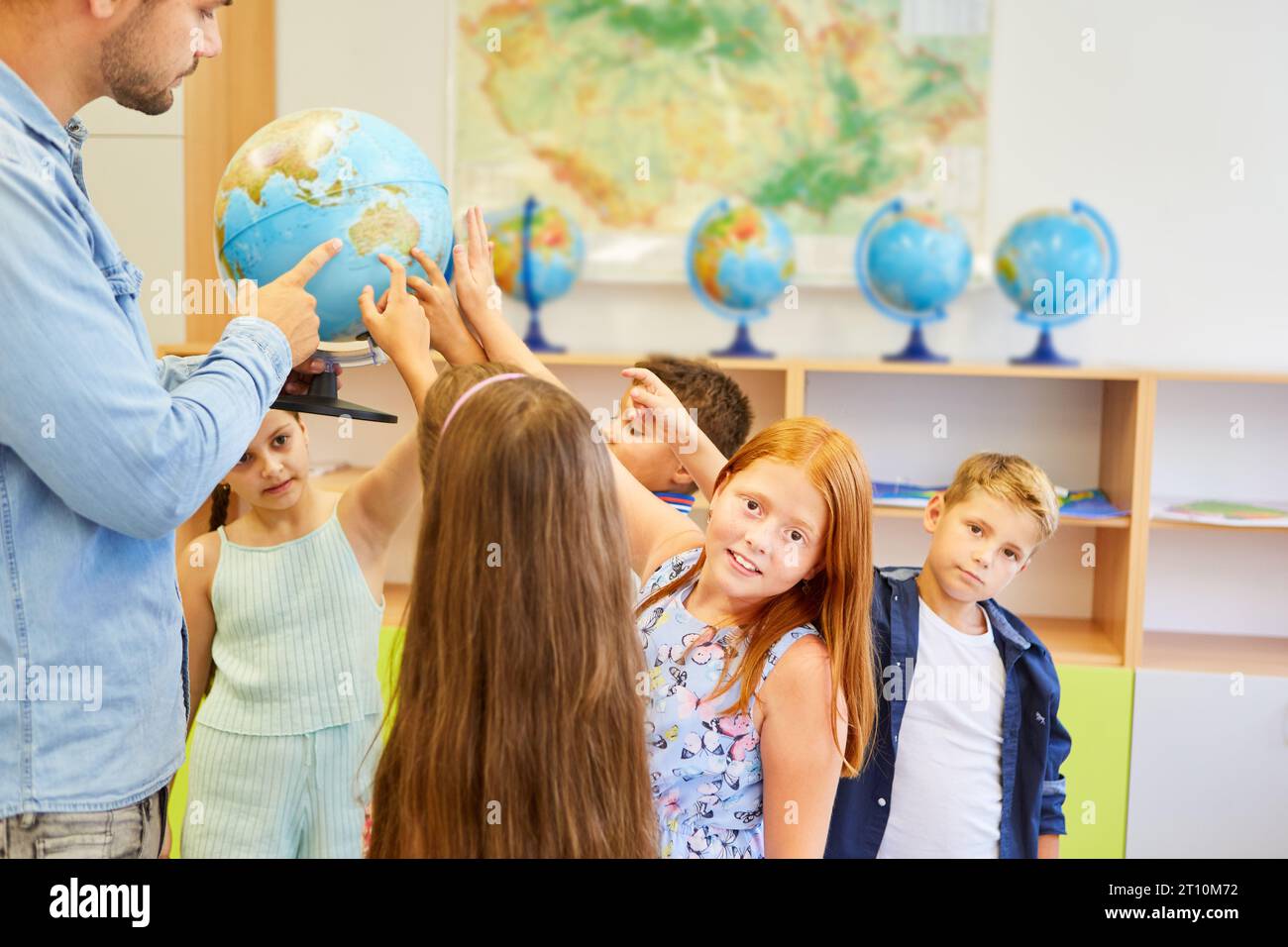 Male teacher holding globe amidst elementary students in geography ...