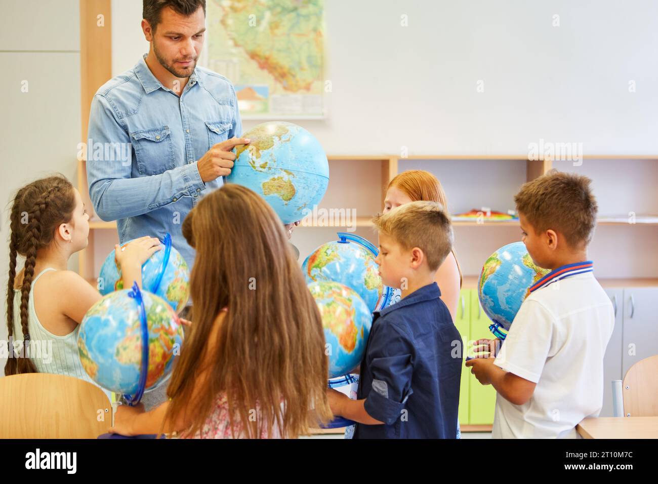 Male teacher explaining maps through globe to elementary students in ...
