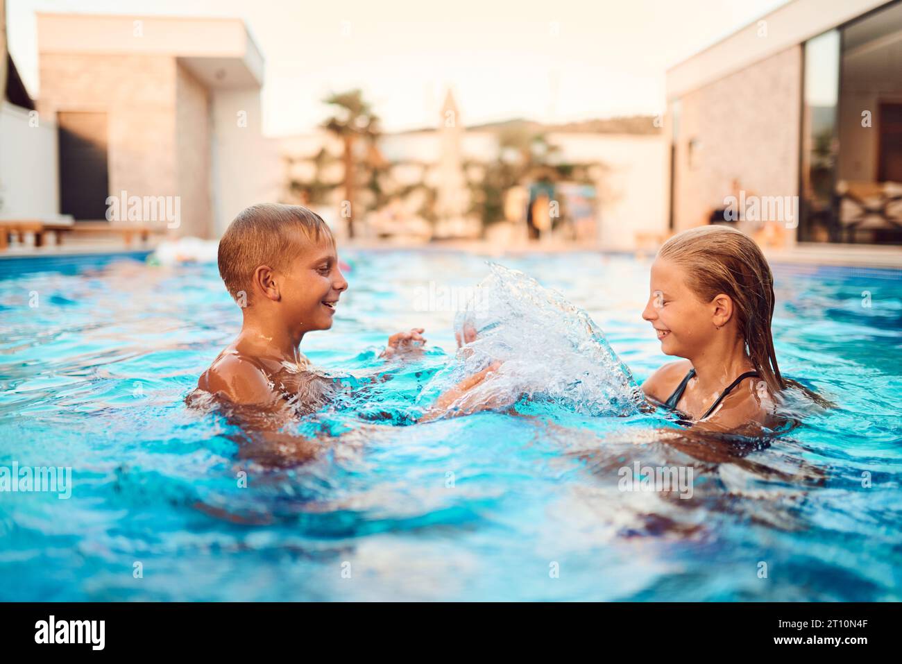 In a sunlit modern villa, a young brother and sister joyfully splash ...