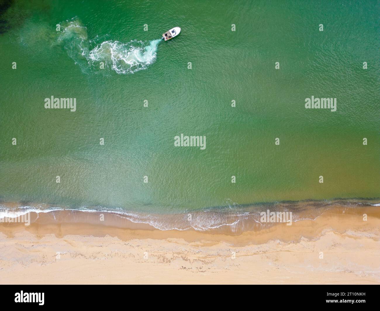 A top-down aerial view of a sandy beach, sea, and motor boat creates a ...