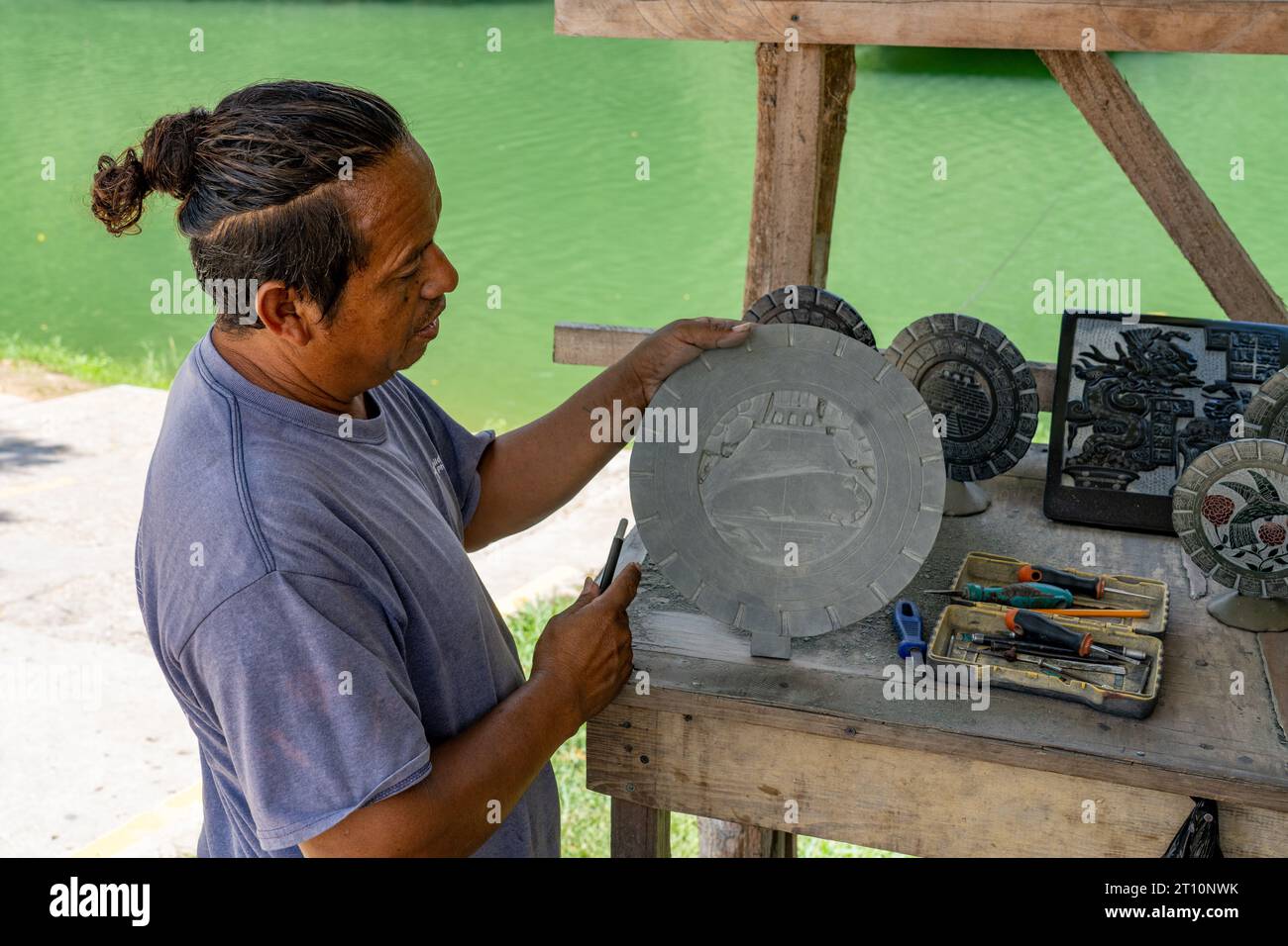 A Mayan craftsman carving a souvenir plaque of a Mayan pyramid on slate ...