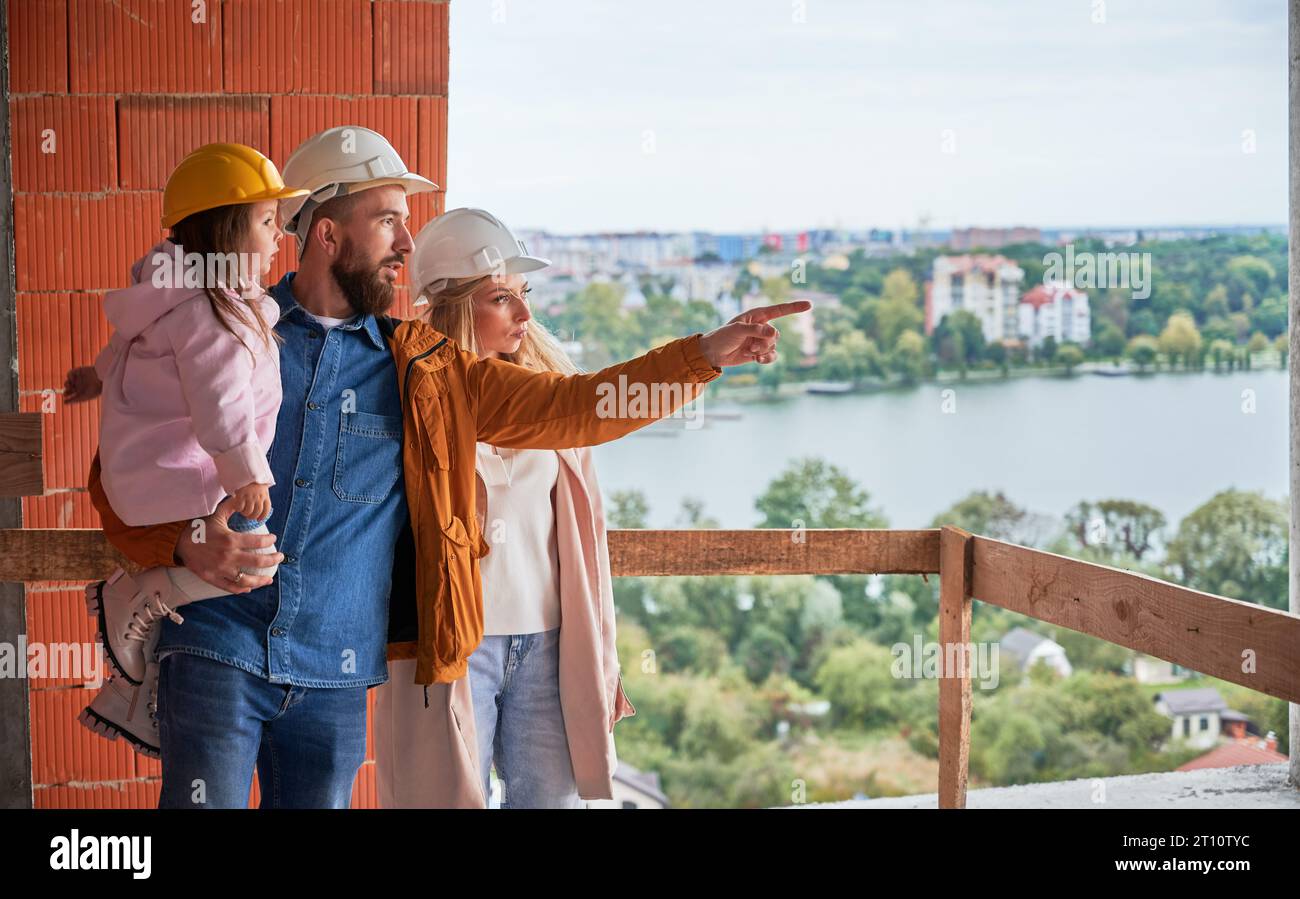 Man in building helmet holding daughter and pointing at something while ...