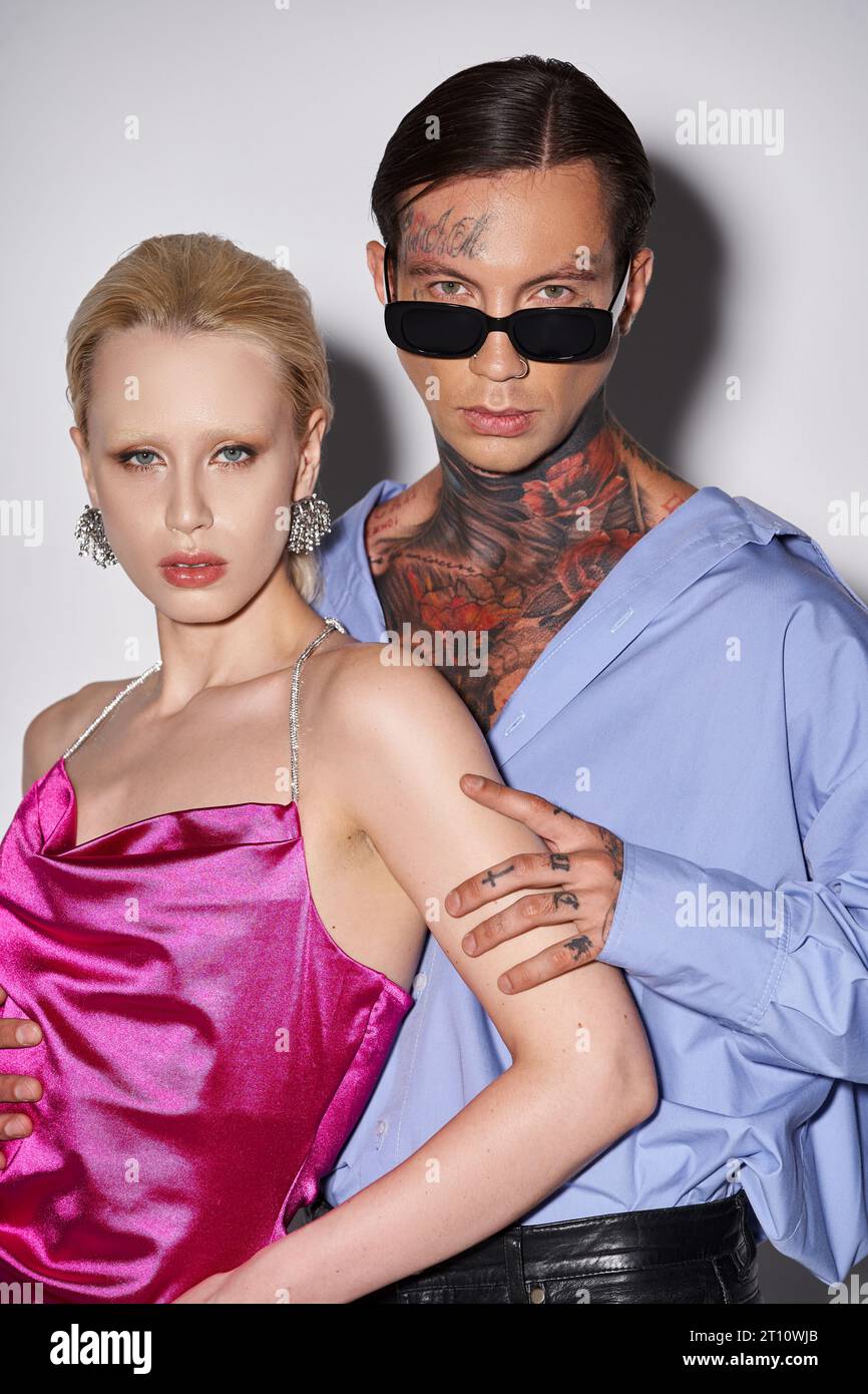 fashionable couple in trendy party attire looking at camera on grey ...