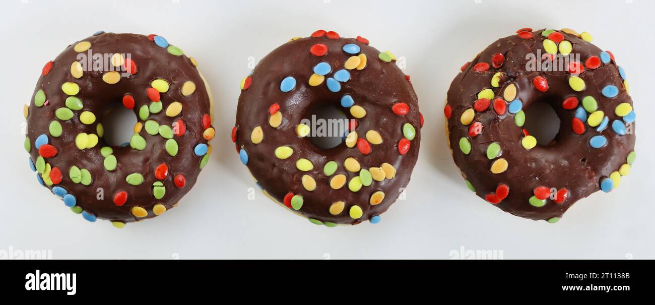 Set of three tasty chocolate donuts with smarties on white background ...