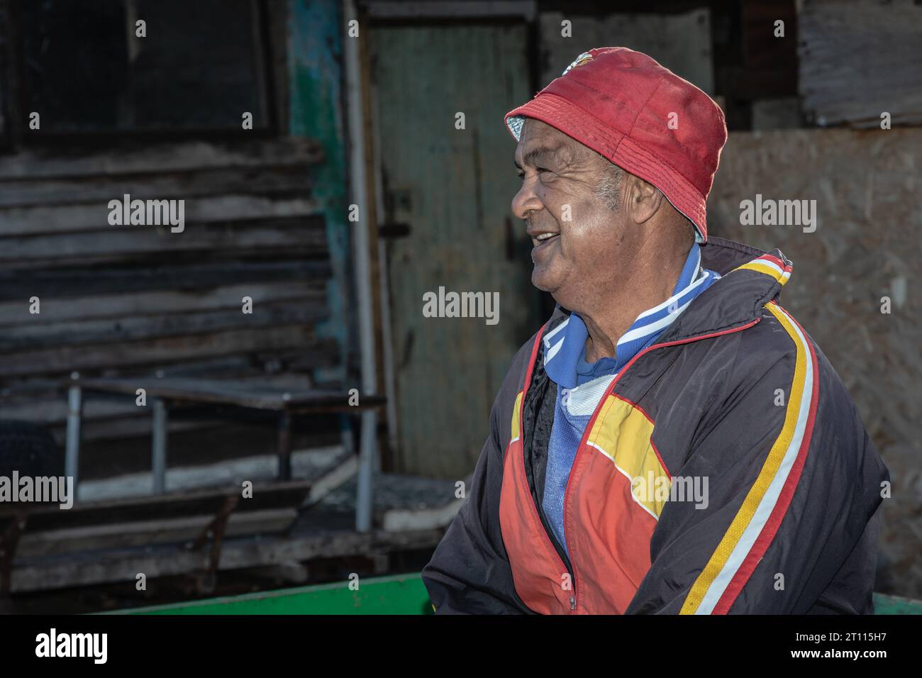 A poor, elderly mixed race man, dressed casually and wearing a red hat ...