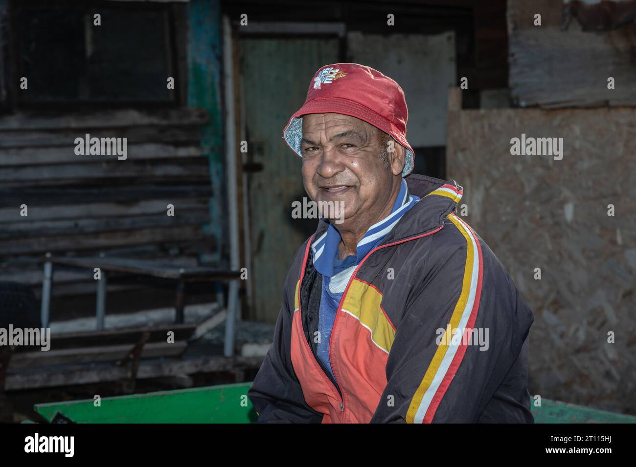A poor, elderly mixed race man, dressed casually and wearing a red hat ...