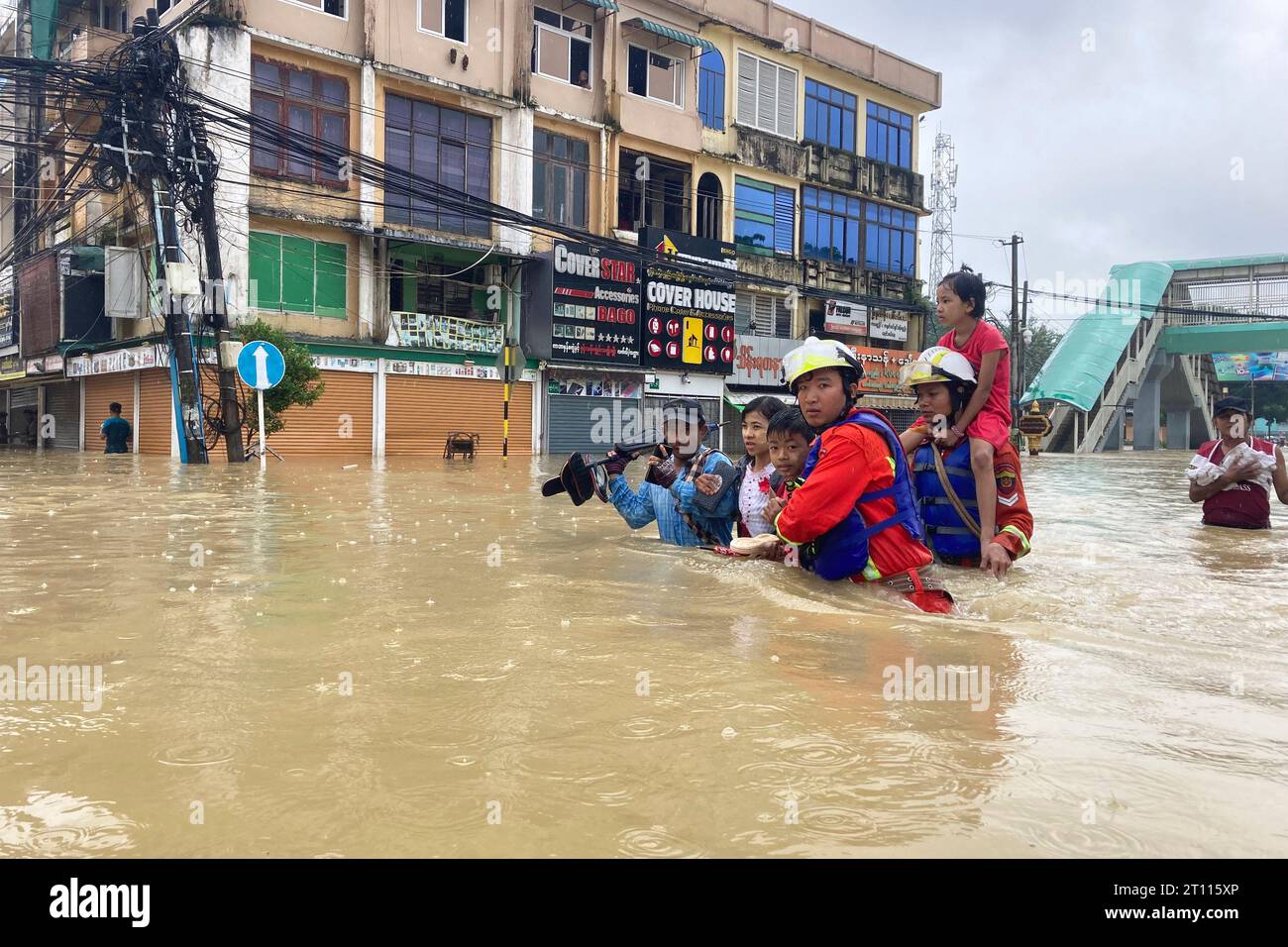 Rescue volunteers and local residents wade through a flooded road in ...