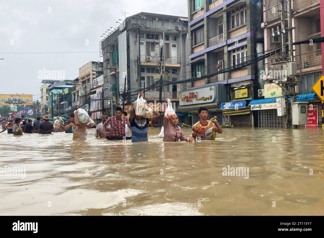 Local residents carrying foods wade through a flooded road in Bago ...