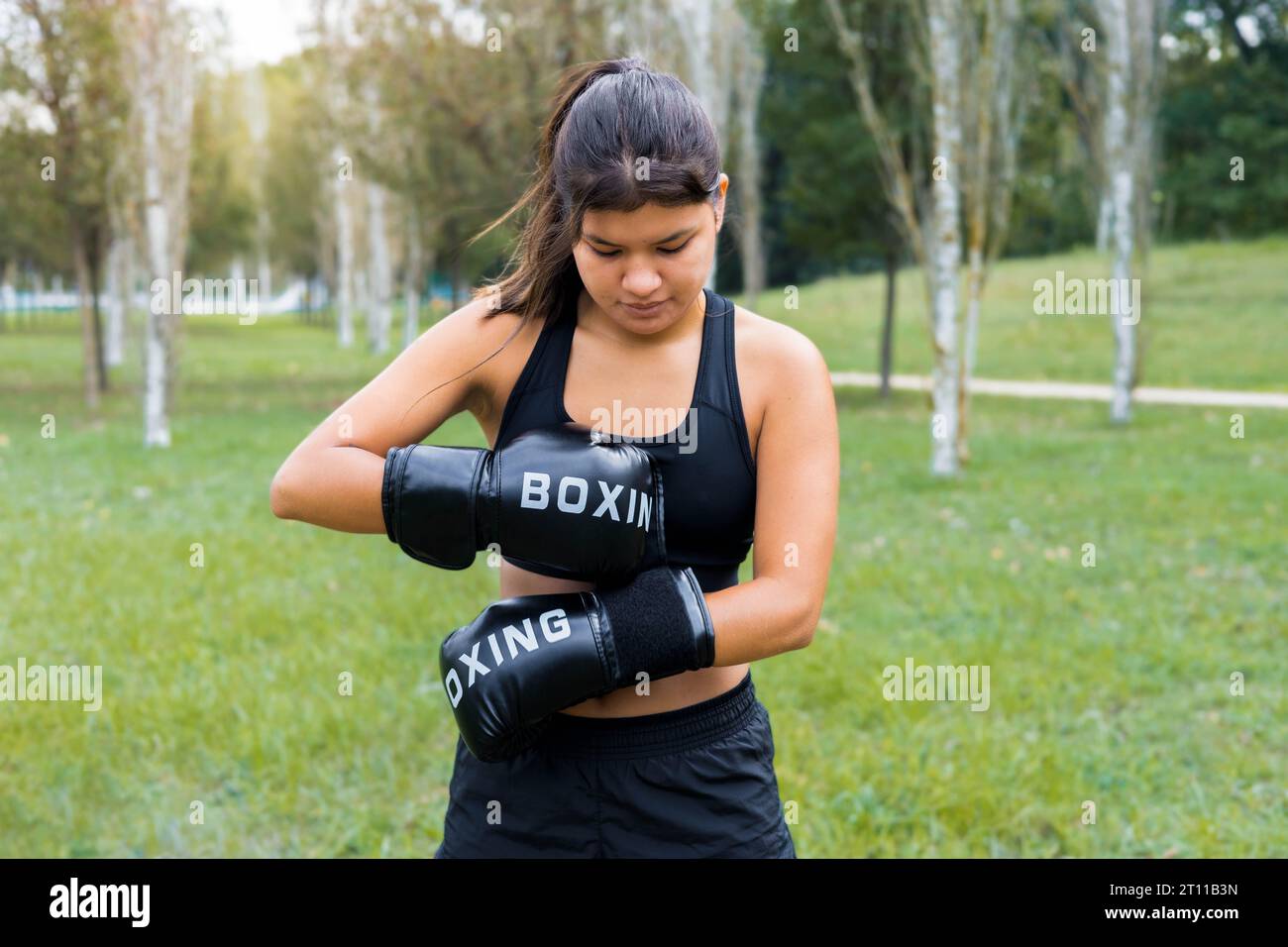 Young latin boxer woman putting on boxing gloves in an outdoor sparring ...