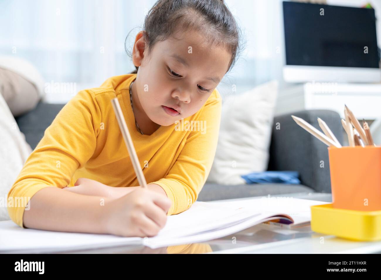 Cute little Asian child girl doing homework writing and reading at home ...
