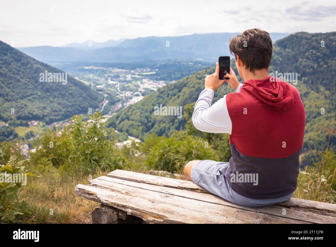Hiking man sitting on a bench at a viewpoint enjoying taking photos of ...