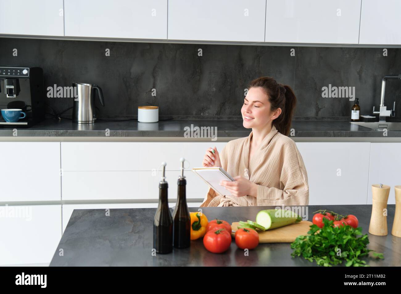 Portrait of woman thinking of menu, sitting in the kitchen and making ...