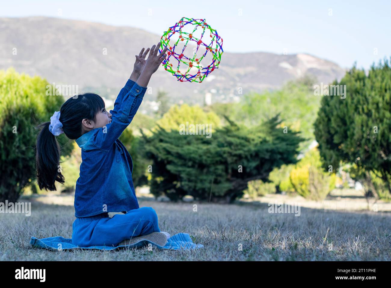 Little girl throwing a ball of many colors into the sky, in a beautiful ...