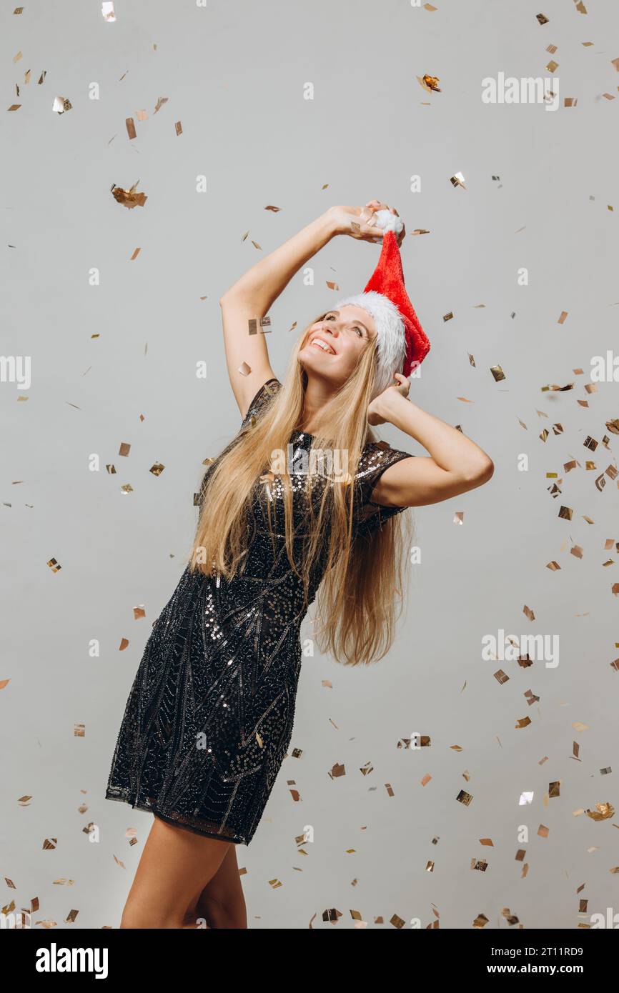 Beautiful blonde Santa girl dancing under glittering confetti. New Year ...