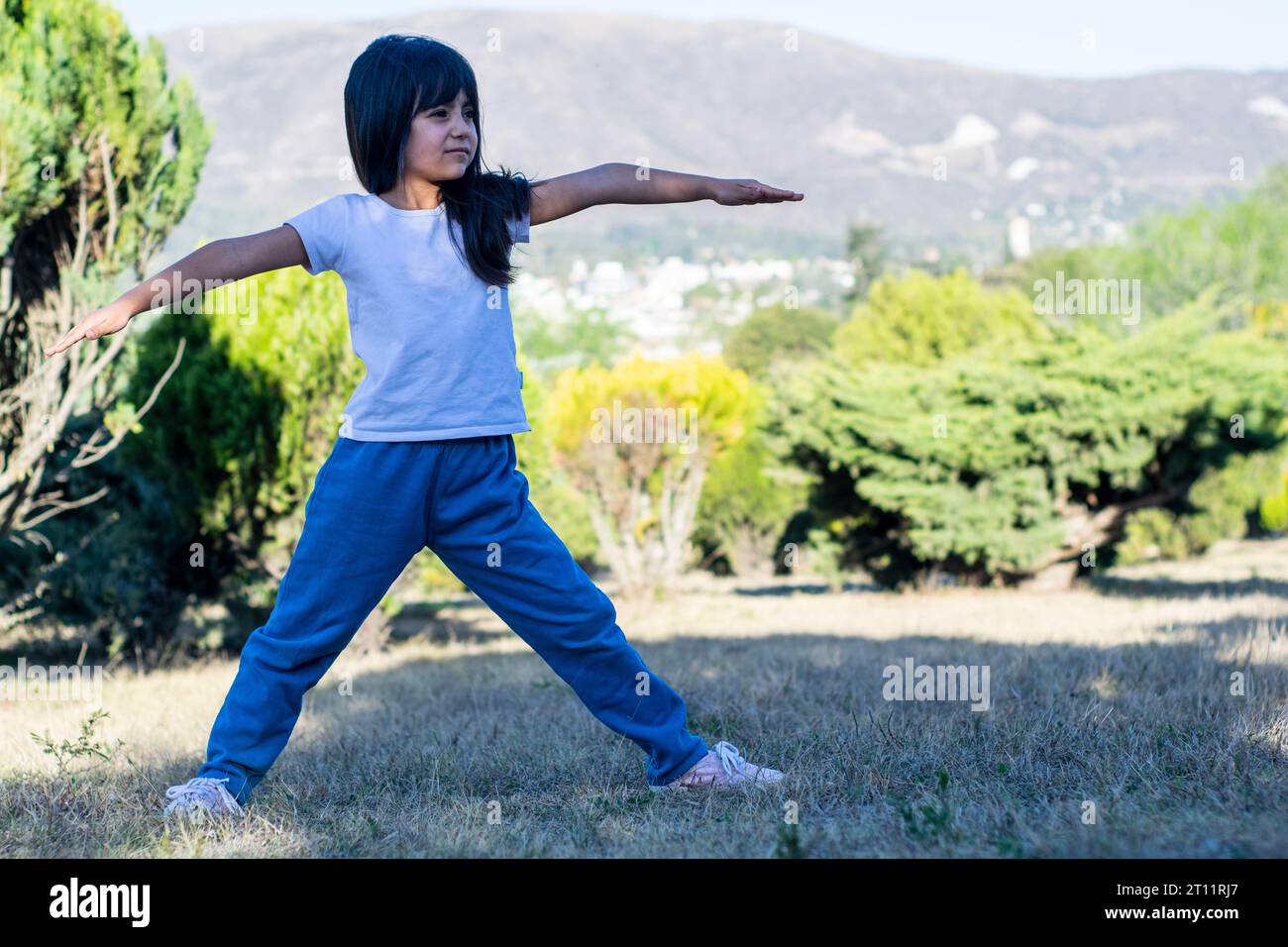 Little girl doing exercises in a beautiful park with bright green ...