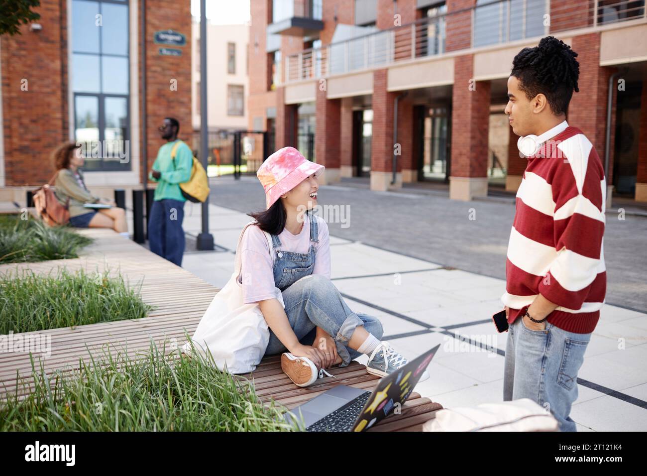 Side view portrait of two smiling young students chatting on campus ...