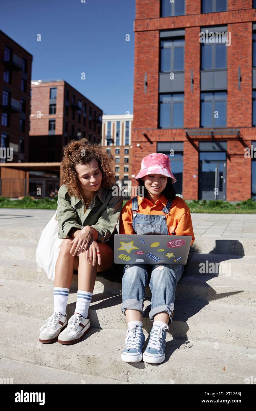 Colorful portrait of two female students using computer outdoors while ...